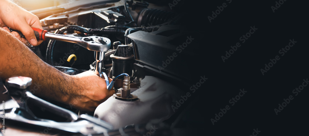 The auto mechanic is fixing the engine of the car with a socket wrench ...