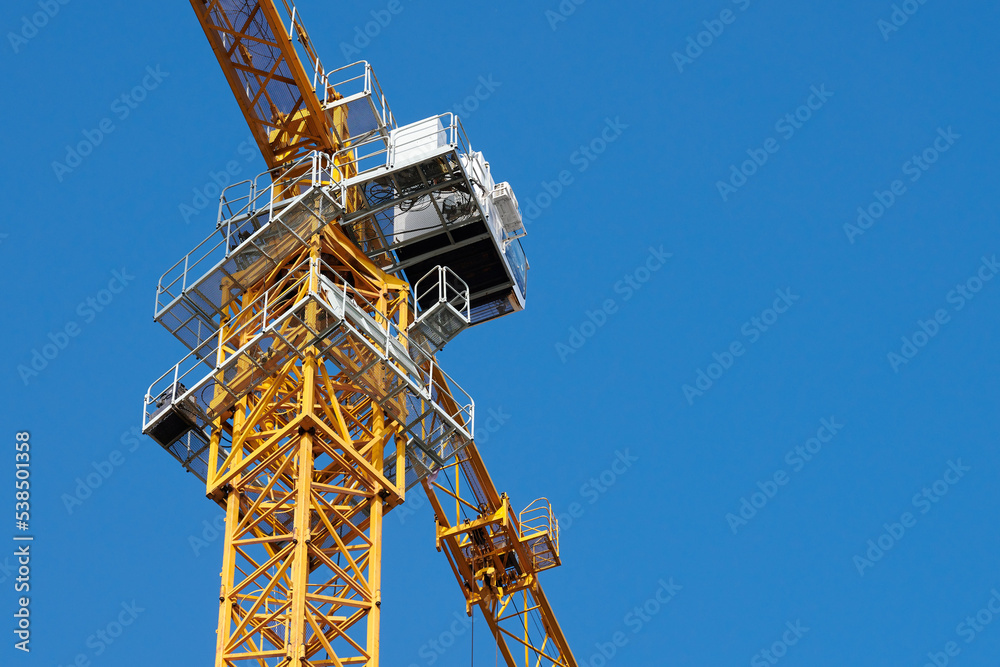 Yellow tower crane with cabin bottom view, blue clear sky background ...