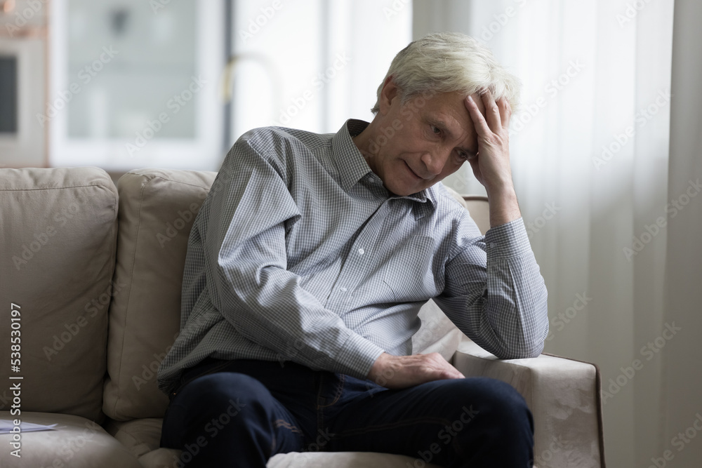 Angry mature hoary man sitting on sofa looking pensive deep in ...