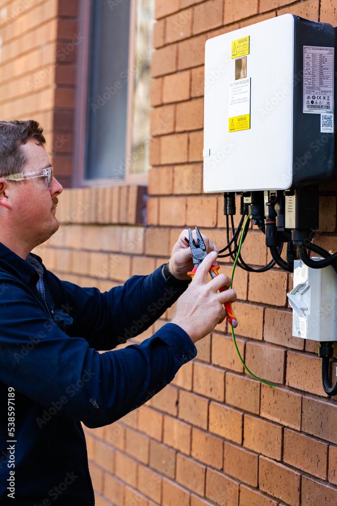 Tradie working as an electrician wiring a solar power control box ...