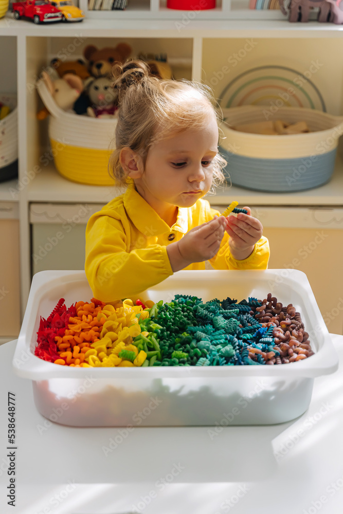 Foto de Child playing with sensory bin with dried pasta in rainbow ...