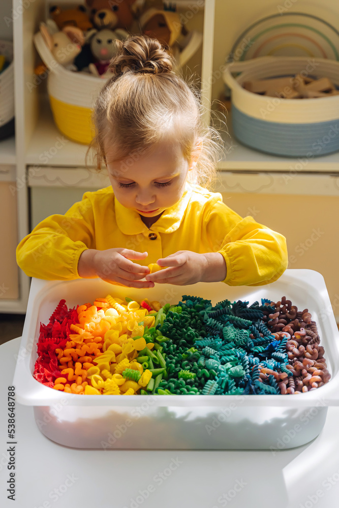 Child playing with sensory bin with dried pasta in rainbow colors. Dyed ...