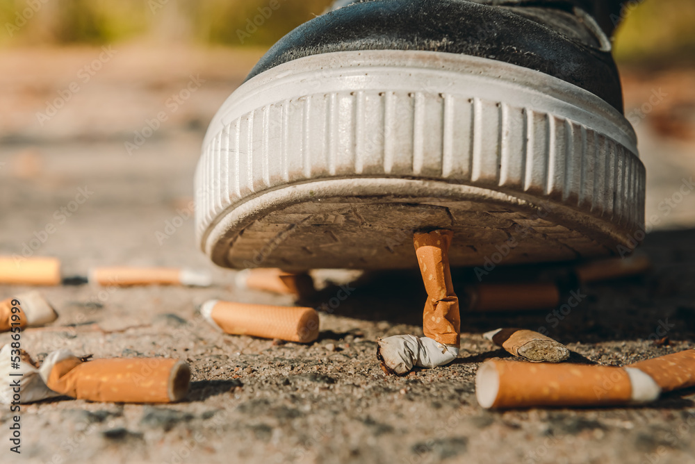 A man puts out a cigarette with his foot. The shoe steps on the ...