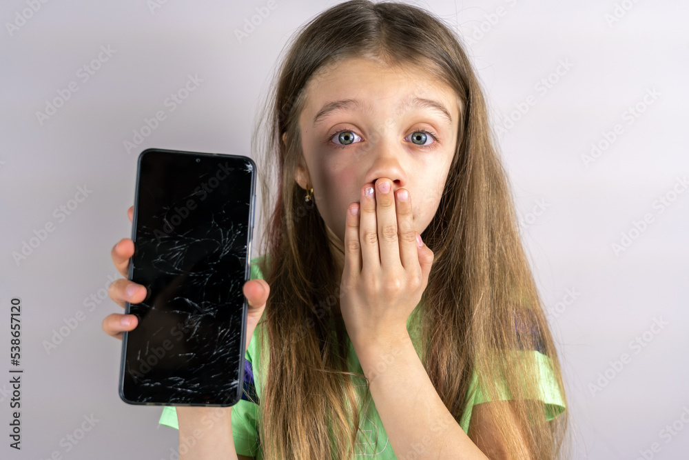 Portrait of terrified child with damaged phone. Upset little girl ...