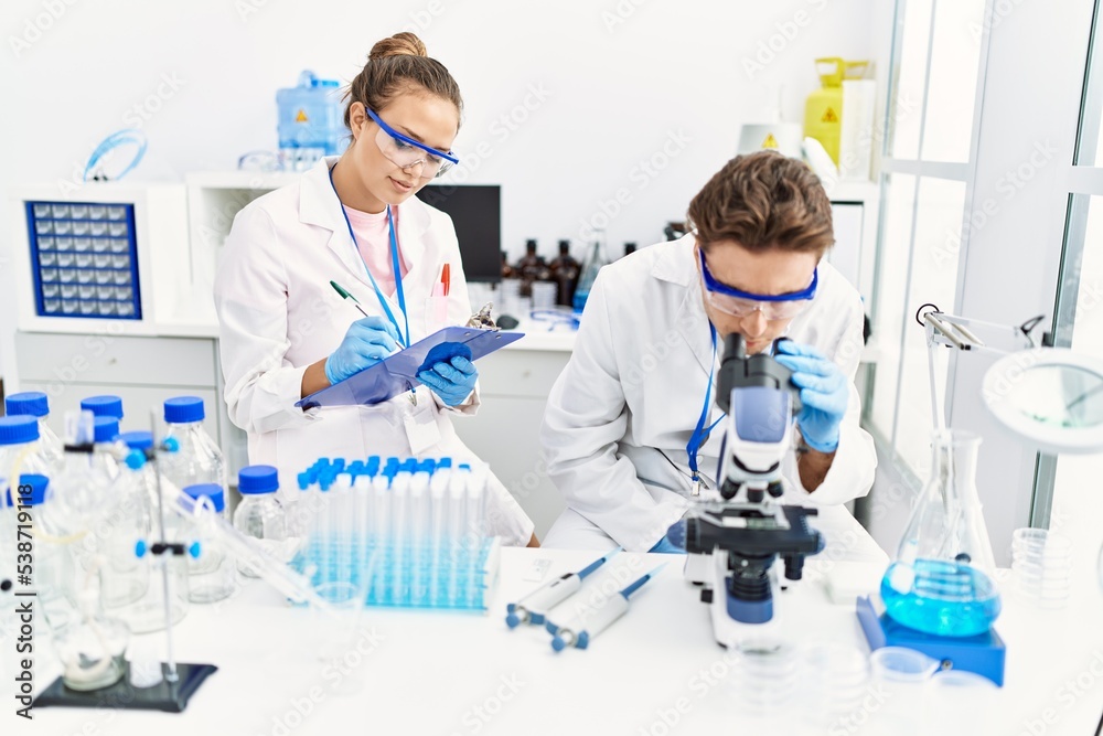Man and woman wearing scientist uniform using microscope write on ...