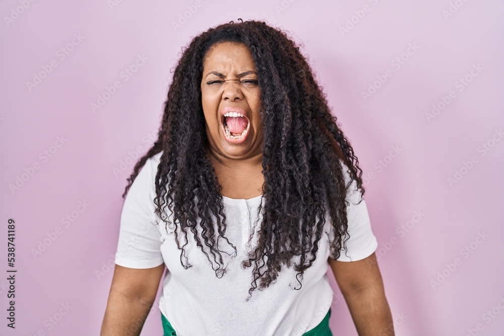 Plus size hispanic woman standing over pink background angry and mad ...