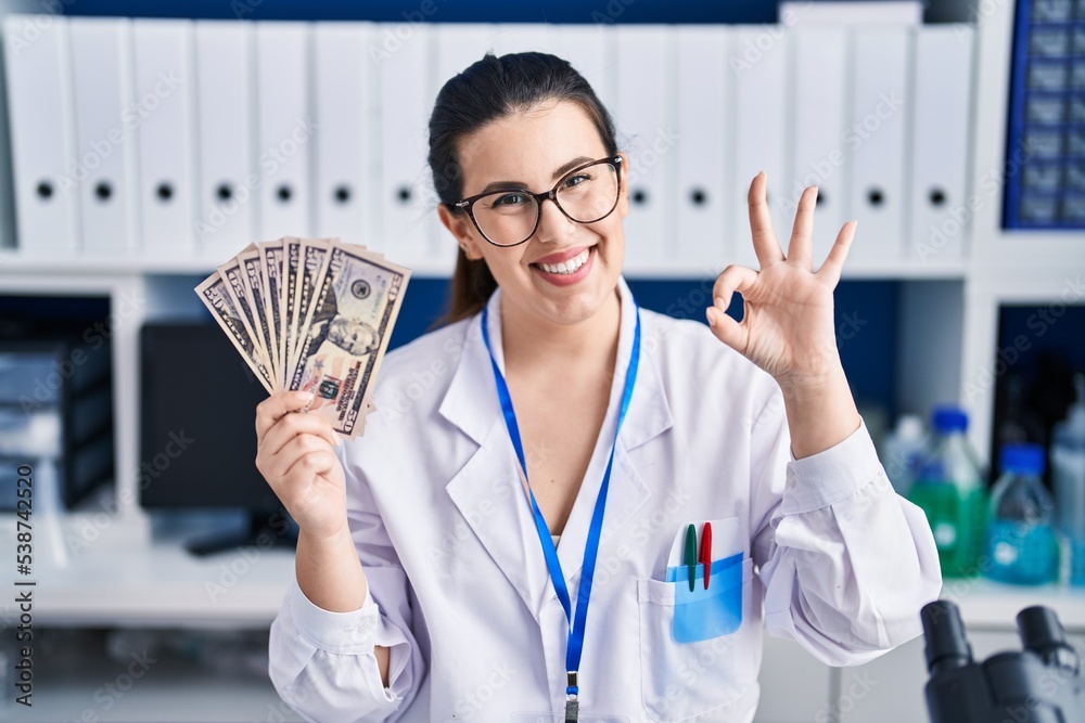 Young brunette woman working at scientist laboratory holding money ...