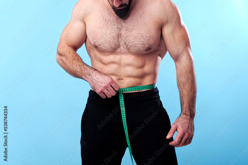 Strong bodybuilder measuring the width of his waist, putting a ...