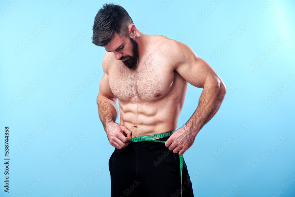 Strong bodybuilder measuring the width of his waist, putting a ...