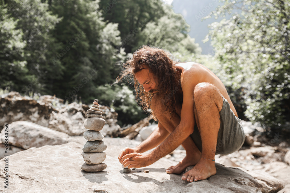 Shirtless man crouching and stacking stones on rock Stock Photo | Adobe ...