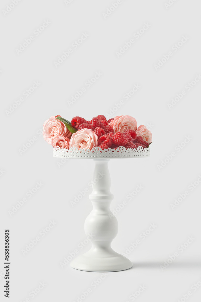 Raspberries with roses on pedestal cakestand against white background ...
