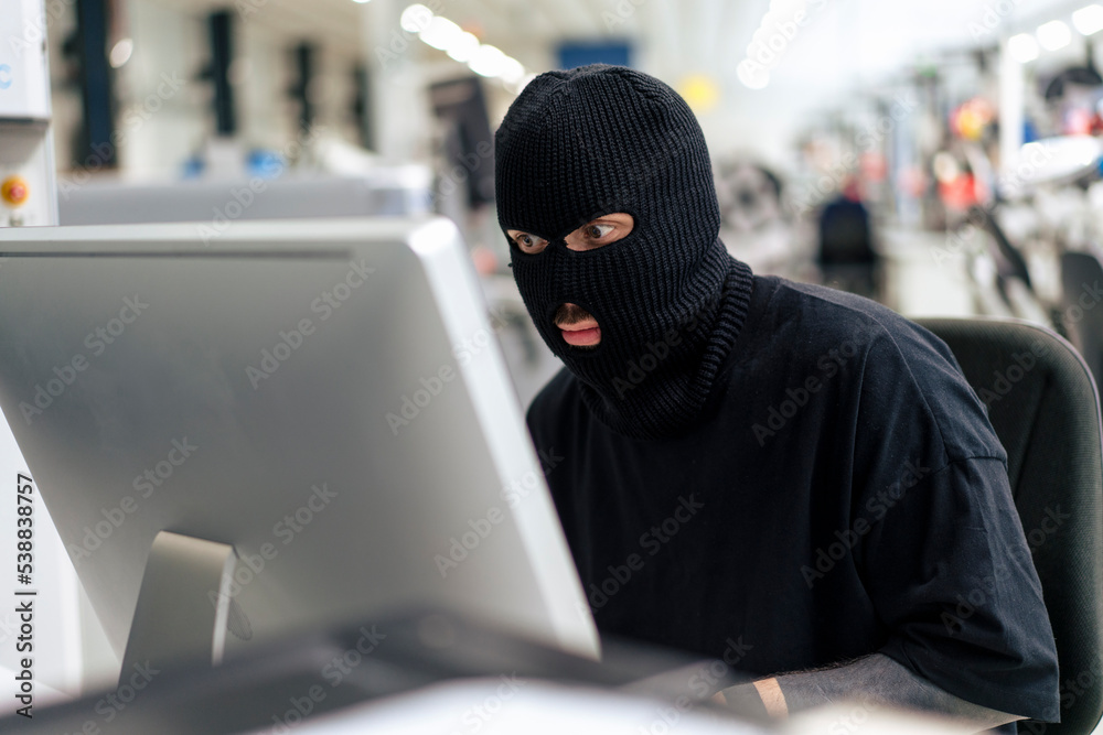 Computer hacker wearing mask using desktop PC at warehouse Stock Photo ...