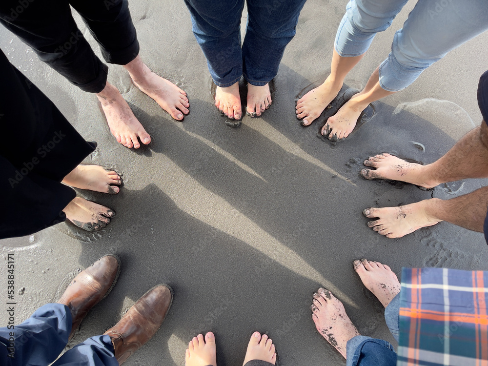 8 people's feet standing in a circle on the sand at a beach with one ...
