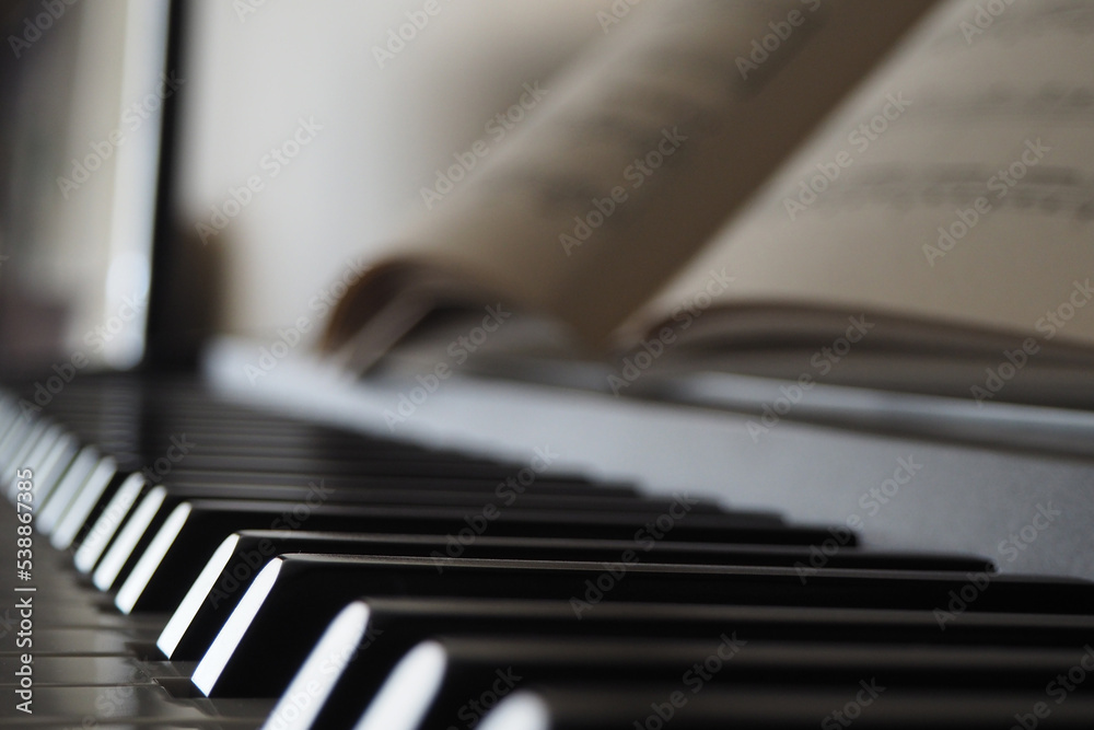 Musical notes on piano. Focused on black piano keys. Blurred sheet in ...