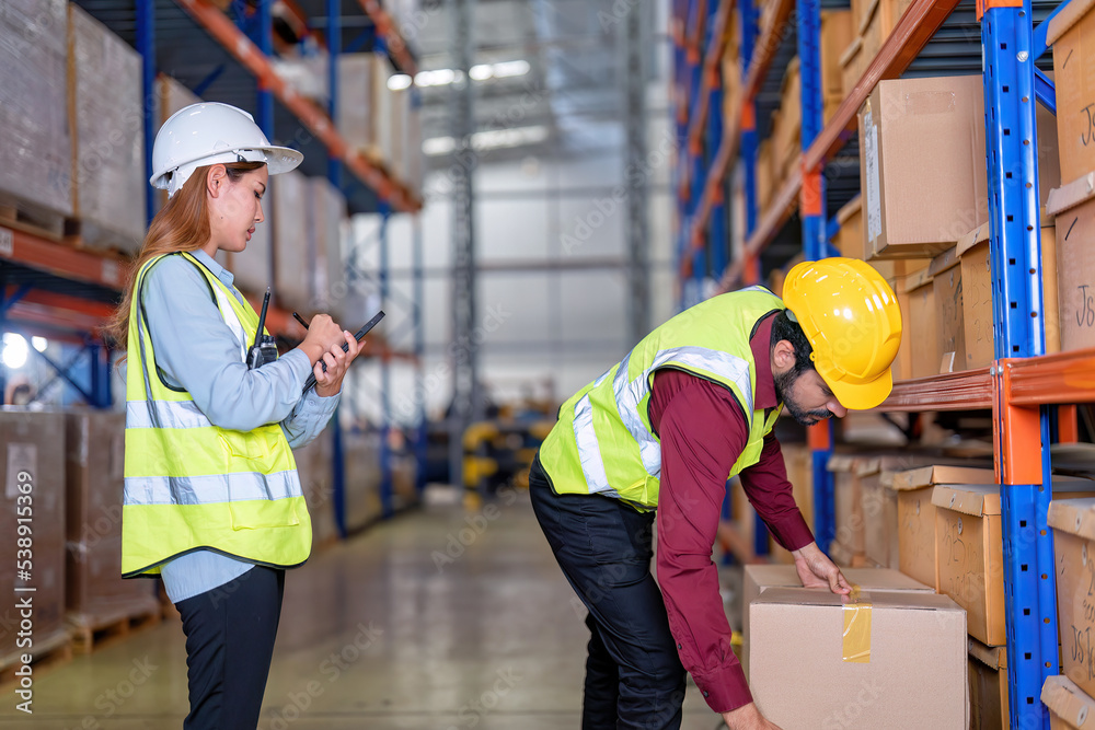 Warehouse worker hold the carton box walk along the steel racking shelf ...