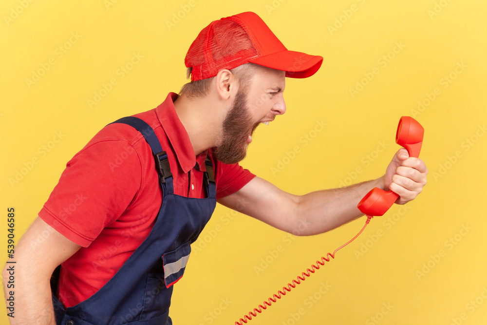 Side view of angry aggressive worker wearing blue overalls screaming to ...