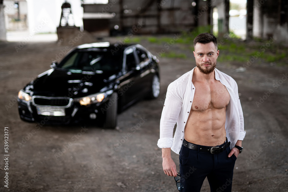 Strong muscular man with car standing. Shirtless bodybuilder with black ...