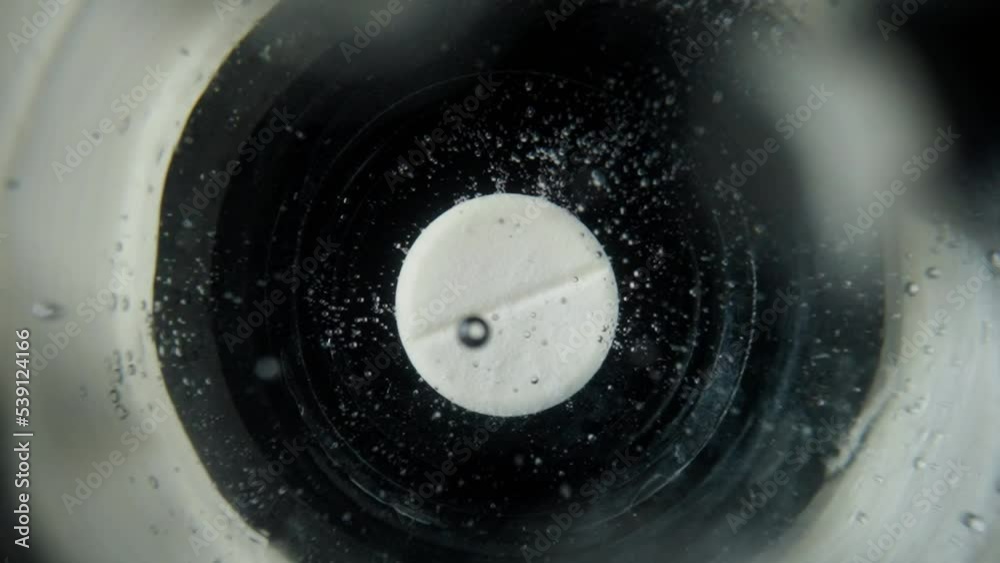 Macro shot of white tablet of soluble aspirin bubbling in glass of ...