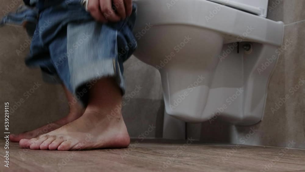 A man goes to the toilet in the toilet, takes off his denim shorts and ...