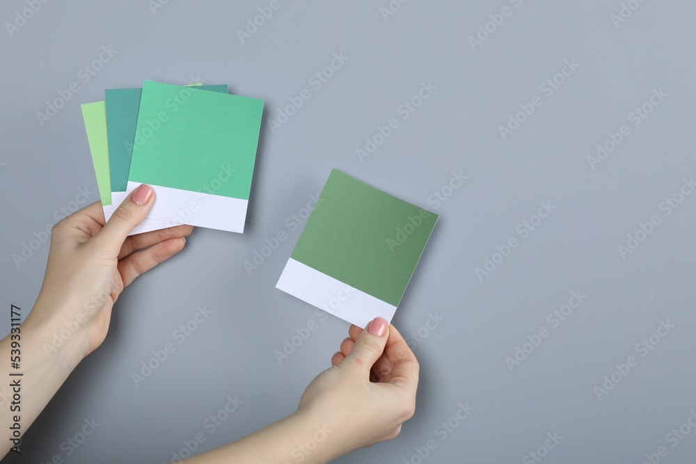 Woman with color sample cards choosing paint shade near grey wall ...
