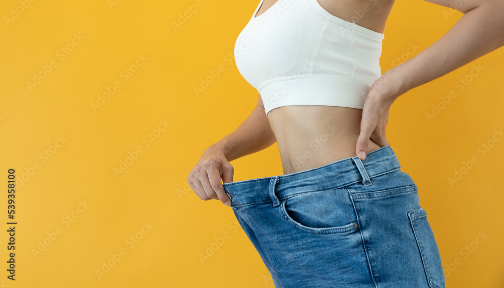 diet, dieting, weight loss. Slim girl in oversized jeans on yellow ...