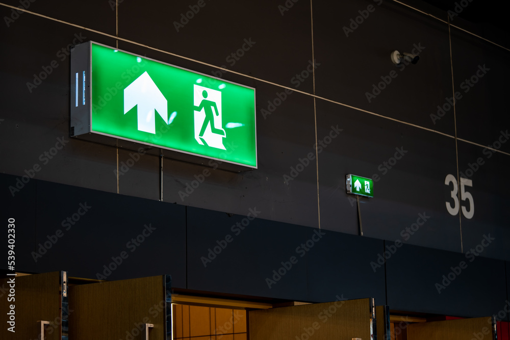 Big Emergency fire exit sign is placed on the black wall over the door ...