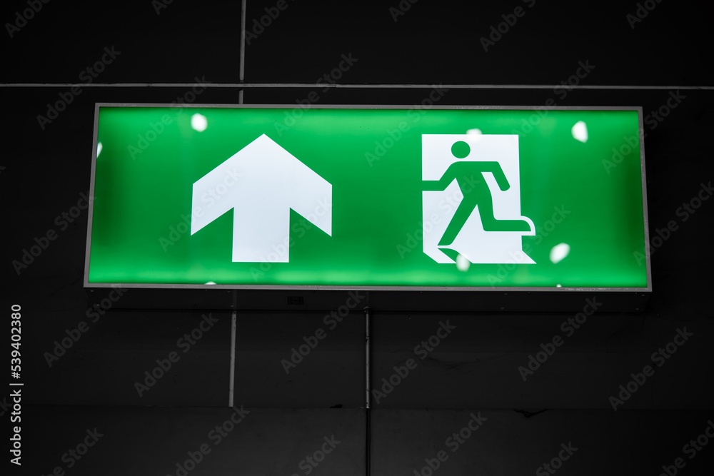 Big Emergency fire exit sign is placed on the black wall over the door ...