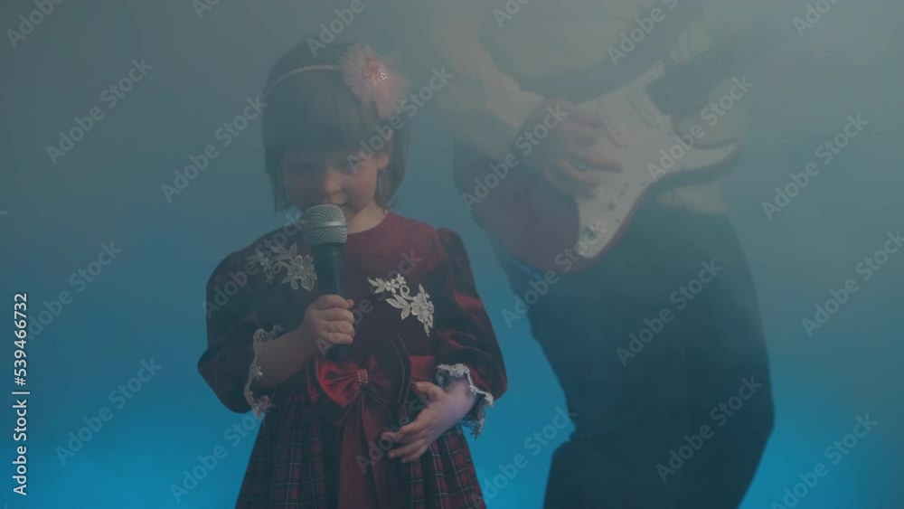 Little girl on stage in vintage dress, she sings into microphone and ...