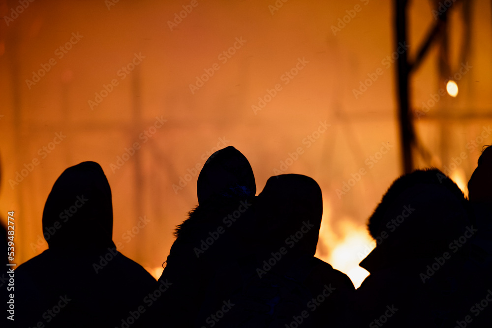 Dark silhouettes of people against the backdrop of a giant raging fire ...
