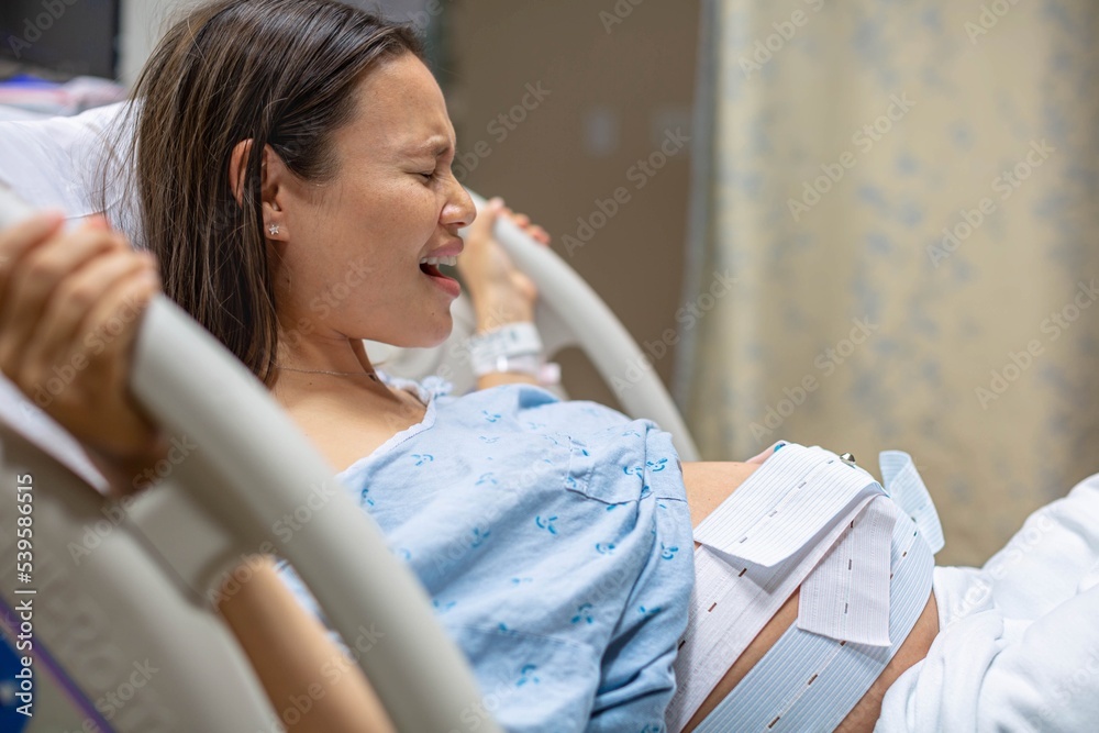 A woman having labor contractions in the hospital, screaming in pain ...