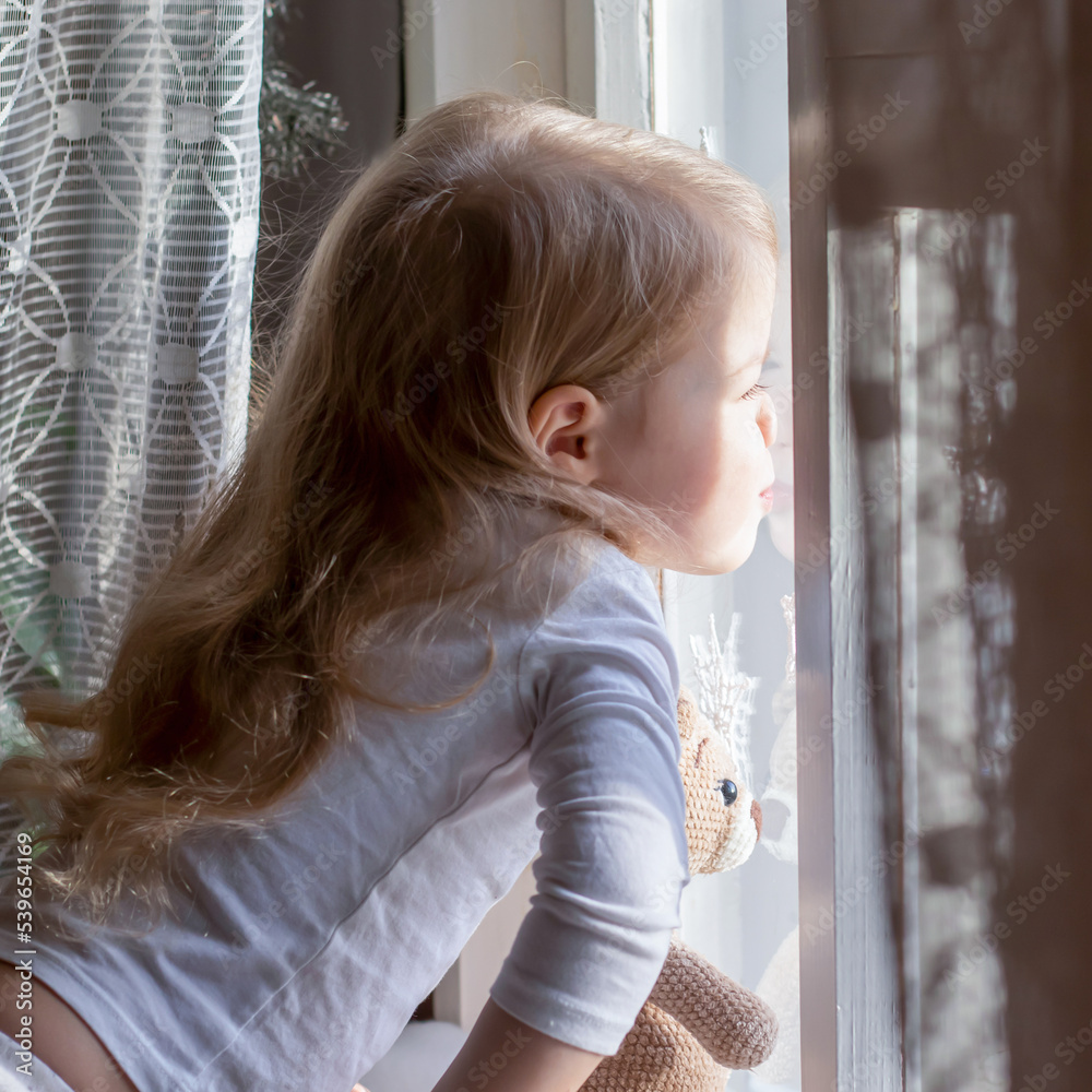 little blonde girl and her toy teddy bear looking out the window ...