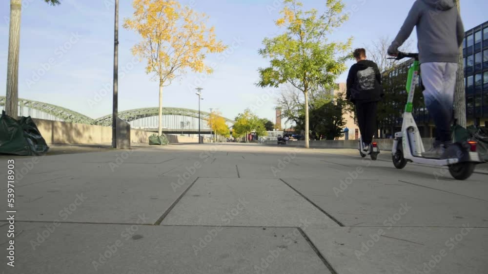 Low dolly forward shot of people riding by on electric scooters in a ...