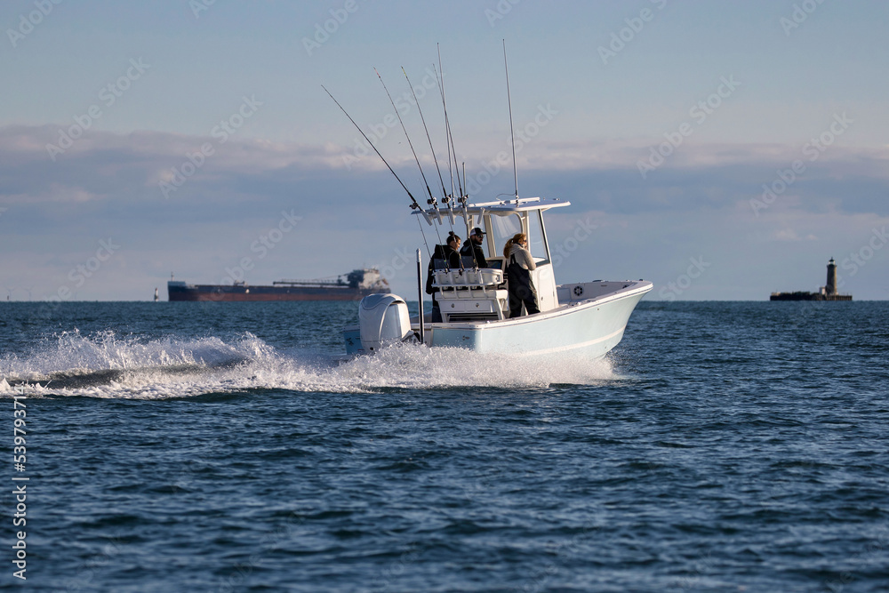 Center console fishing boat heading toward a lighthouse with a ship in ...