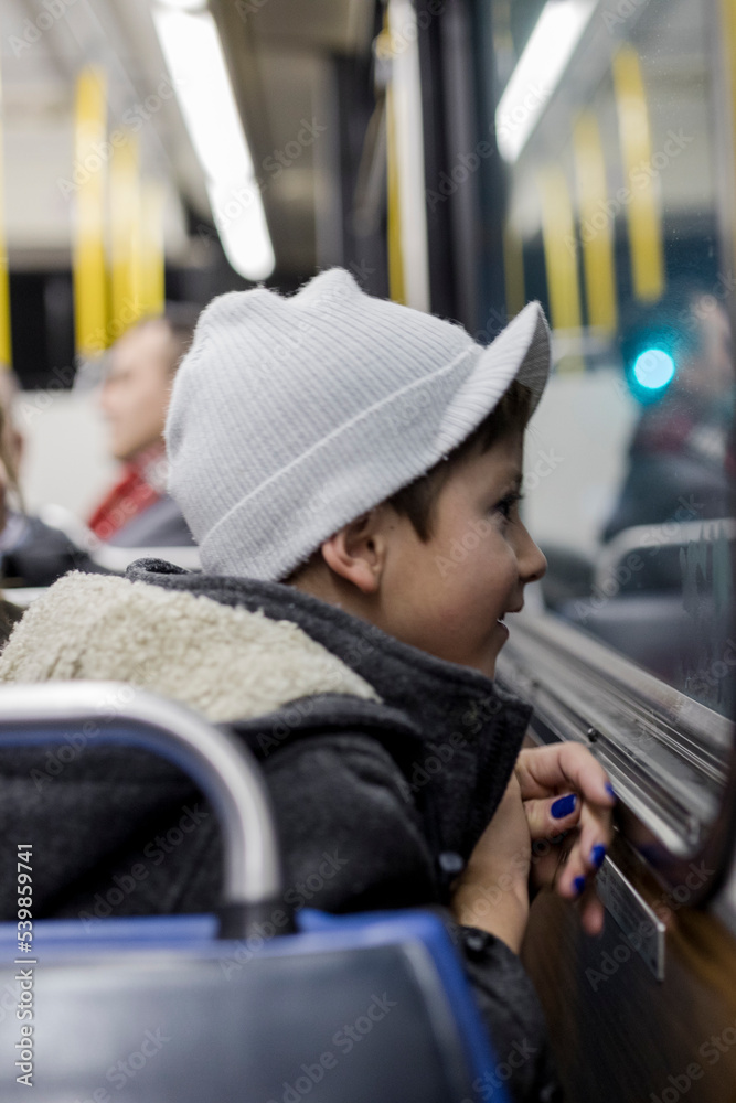 Curious boy riding bus with mother and brother, looking out window ...