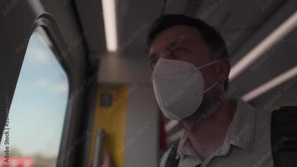 A sad, tired man in a mask traveling on a railroad train, standing at ...