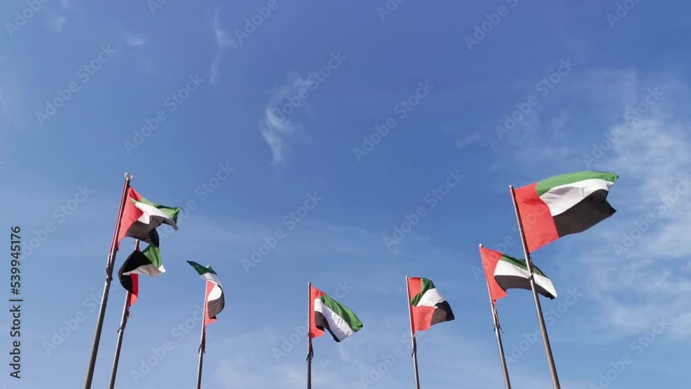 United Arab Emirates flags waving in wind in blue sky background. Seven ...
