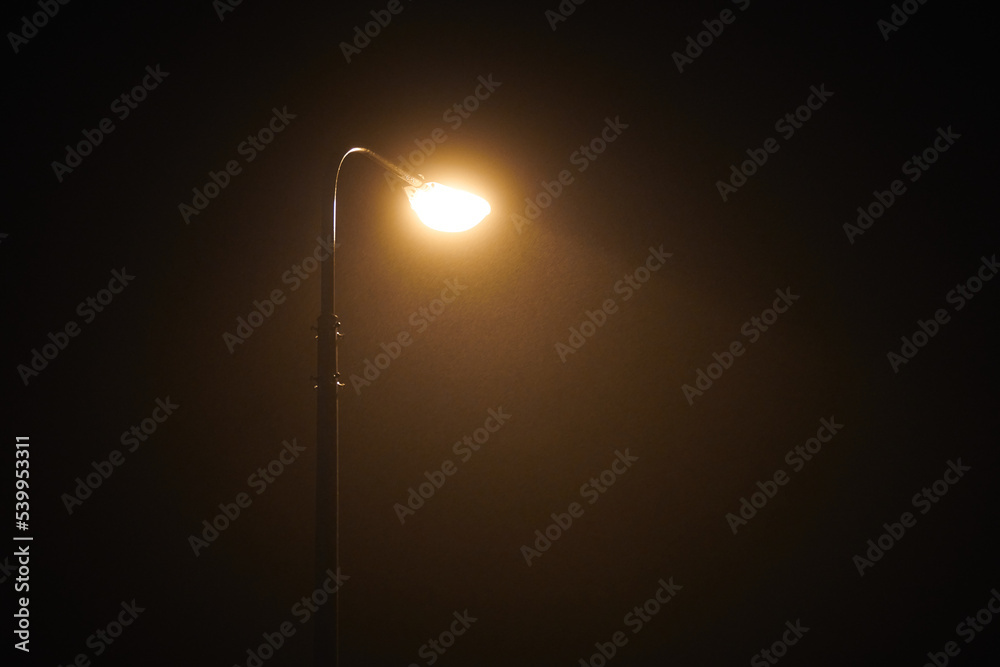 One night lamppost shines with faint mysterious yellow light through ...