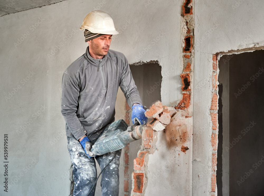 Worker in protective helmet with perforator completing deconstruction ...
