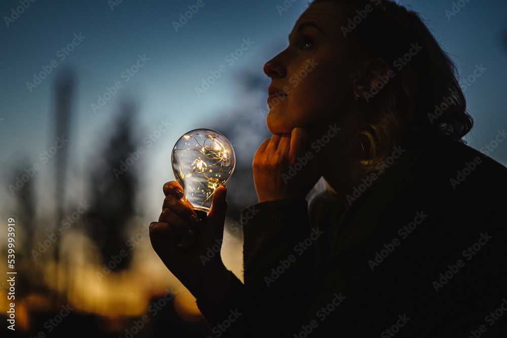 young worried woman holding bright shining lightbulb in her hands ...