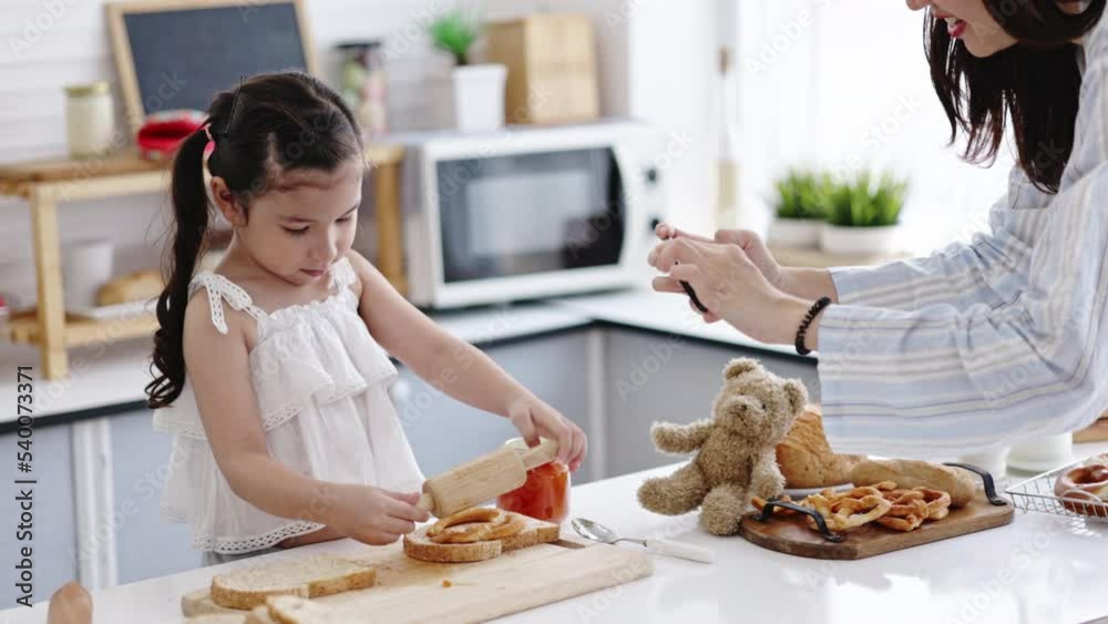 toddler girl is learning to cook bread in the kitchen with her mom with ...