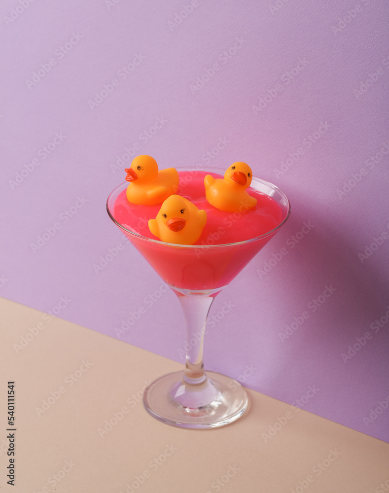 Cocktail glass with rubber ducks on two tone pastel background. Visual ...
