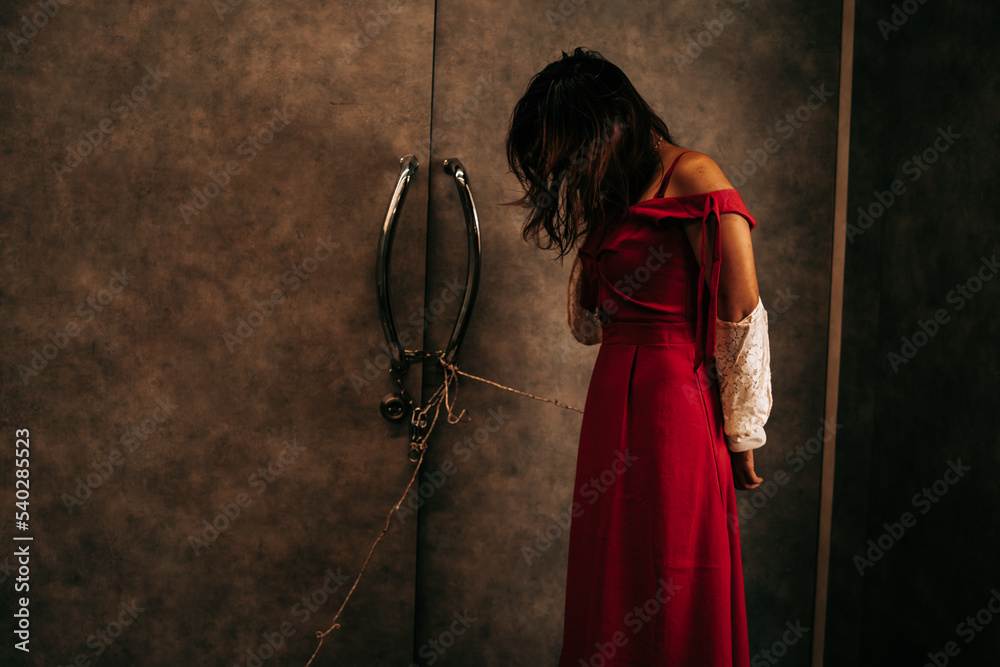 A woman wearing a red dress is standing in a scary room by a villain ...