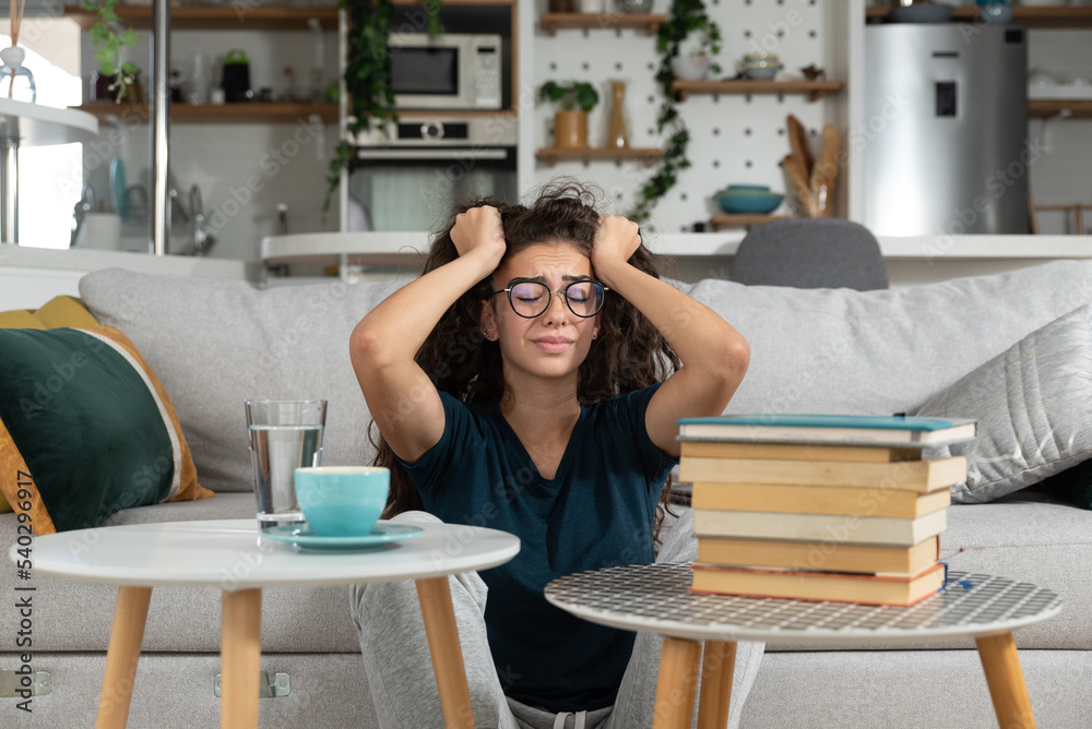 Young frustrated school girl sitting on floor with pile of books ...