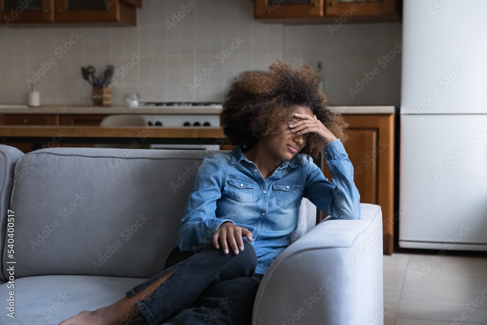 Upset African 20s girl crying seated alone on sofa, cover face with ...