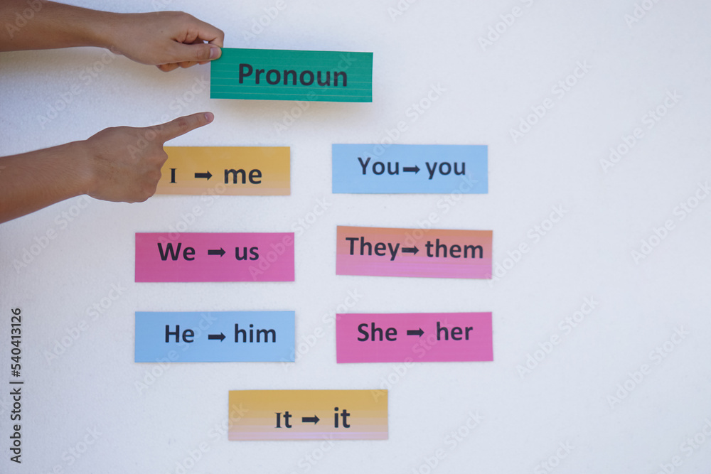 Closeup hand holds green paper card with word " Pronoun" on it. Blurred ...