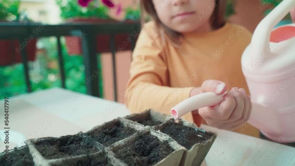 Little girl watering planted seeds from a watering can. Kid plants and ...