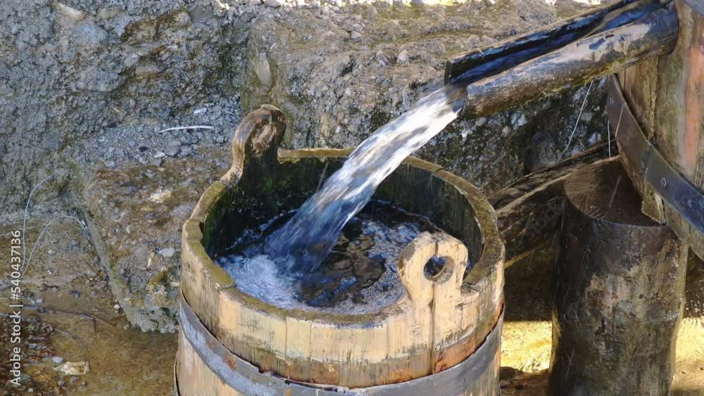 Water pouring into wooden bucket from a barrel with old-fashioned ...