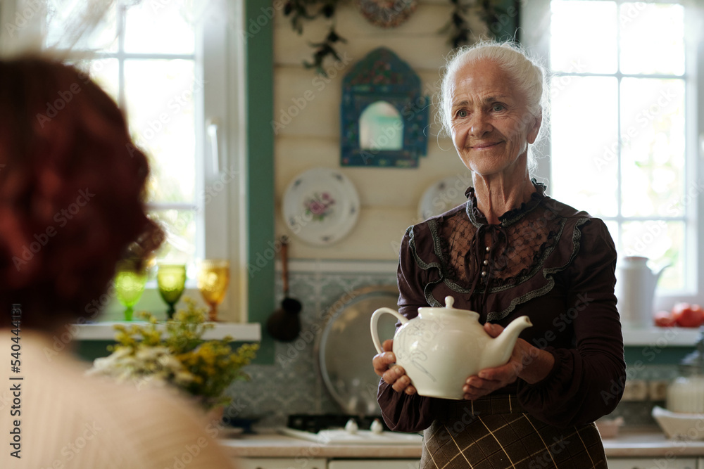 Happy grandmother with white porcelain teapot moving towards her ...