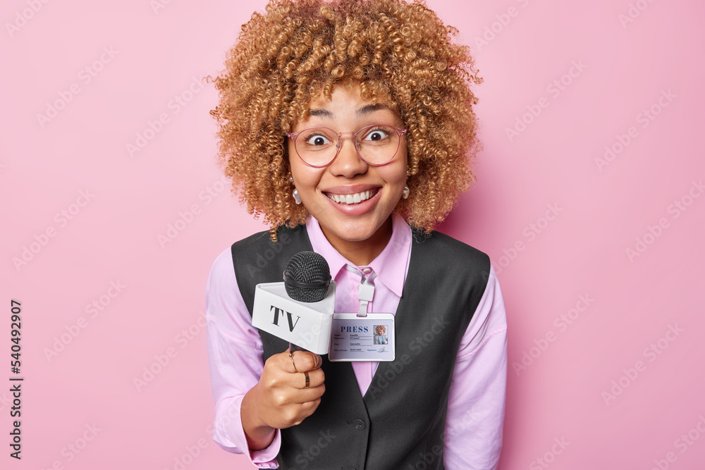 Glad female reporter holds microphone wears transparent eyeglasses and ...