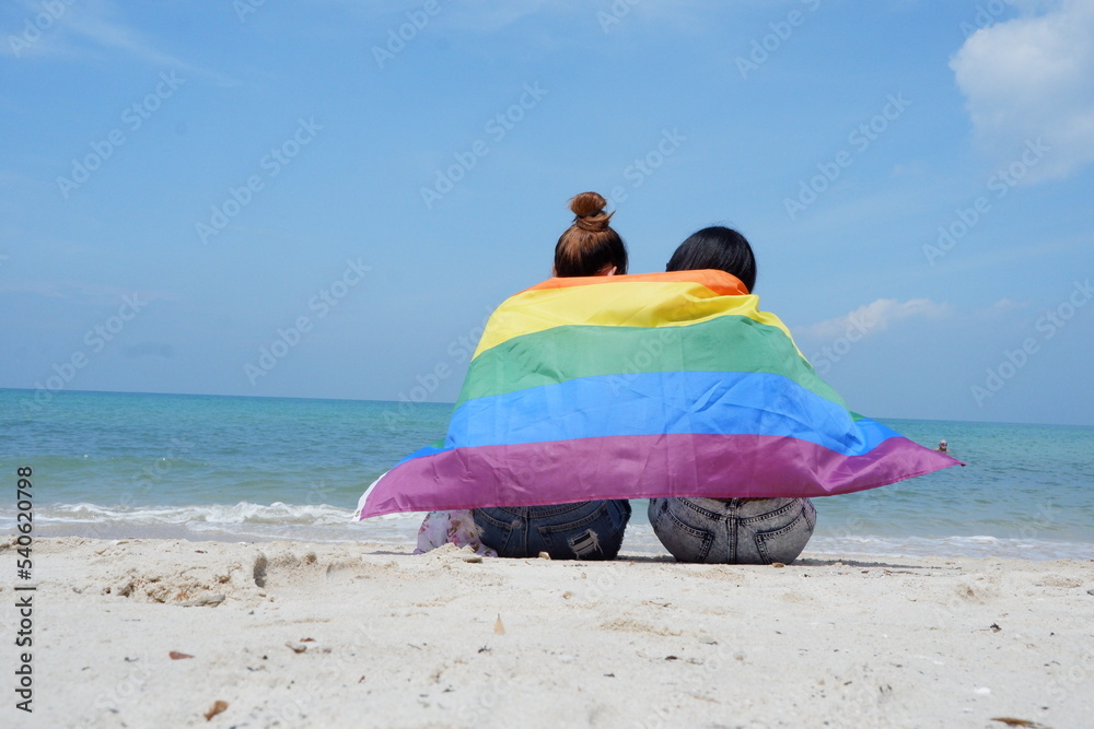 A lesbian couple holding a rainbow flag of LGBT symbols sits on the ...